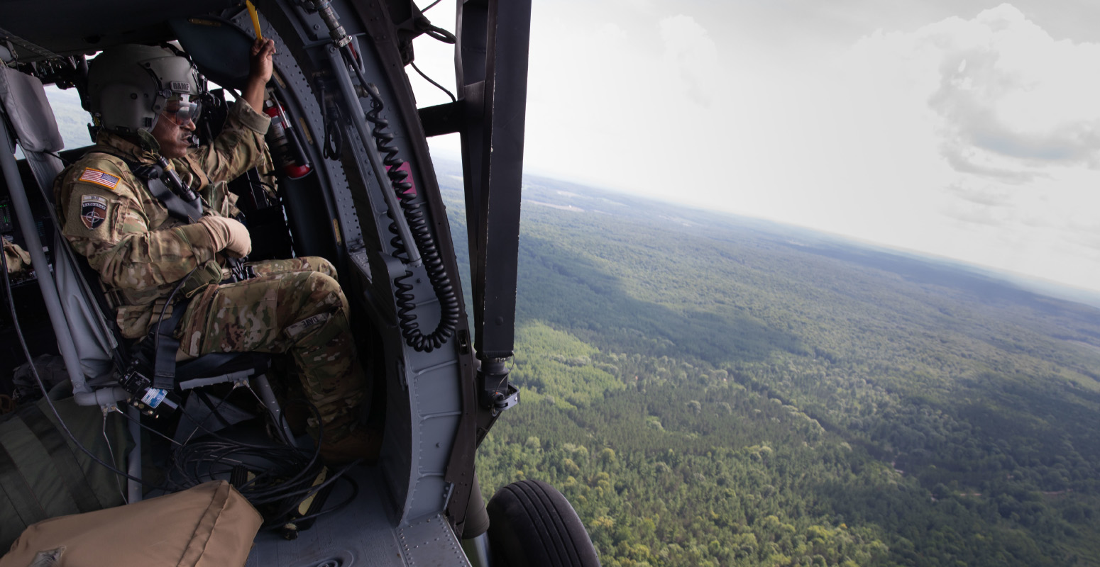 Military person in naval aircraft flying with the doors open.