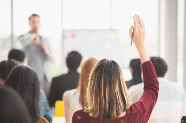 Professionals learning in classroom with instructor; Woman raising her hand.