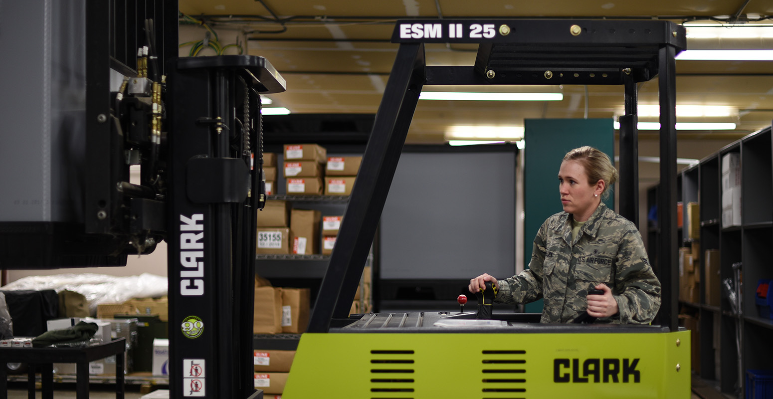A women in military uniform using a forklift with shelves and boxes ...